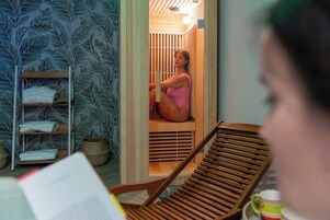 Uma sala de sauna com um banco de madeira, uma prateleira com toalhas dobradas e uma pessoa sentada.