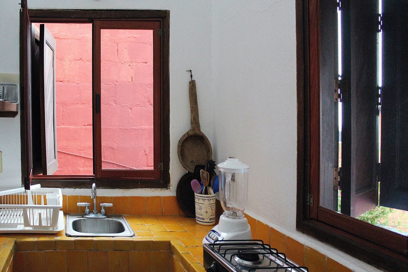 Cozinha com pia, janela e um espremedor no balcão, além de uma colher de pau pendurada.