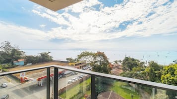 Uma varanda com vista para a praia, um posto de gasolina e carros estacionados.