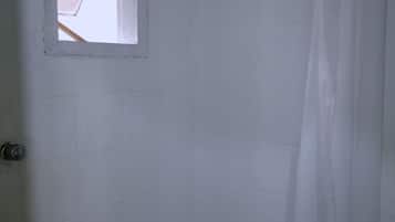 Um banheiro pequeno e fechado, com paredes em azulejo branco, uma janela e um cortina de chuveiro.