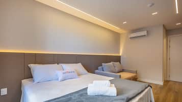 Quarto de hotel com cama, sofá, ar-condicionado fixado na parede e uma porta.