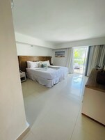 Quarto de hotel com uma cama grande, uma mesinha de cabeceira, uma escrivaninha e vista para o exterior.