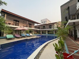 Piscina com espreguiçadeiras e área de estar coberta, cercada por edifícios com varandas.