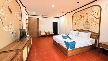 Quarto de hotel com uma cama grande, uma escrivaninha com computador, um guarda-roupa e um painel decorado com flores e pássaros.