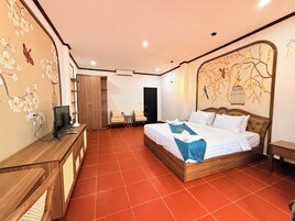 Quarto de hotel com uma cama grande, uma escrivaninha com computador, um guarda-roupa e um painel decorado com flores e pássaros.
