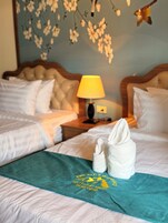 Quarto de hotel com duas camas, uma mesinha de cabeceira com abajur e um detalhe decorativo na parede.
