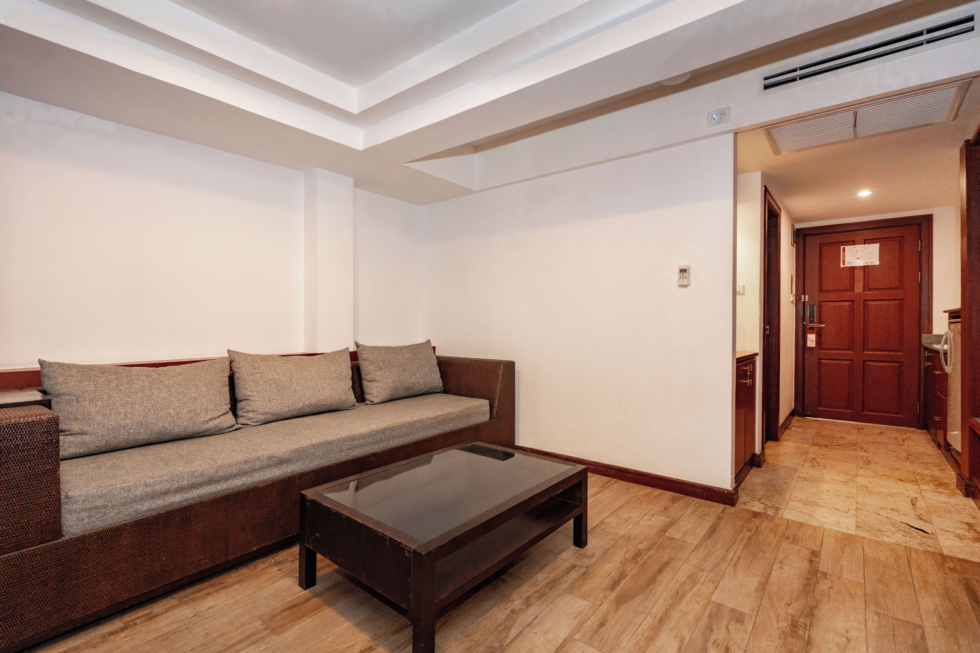 Uma sala de estar com sofá, mesa de centro, piso de madeira e uma porta que dá para outro cômodo.