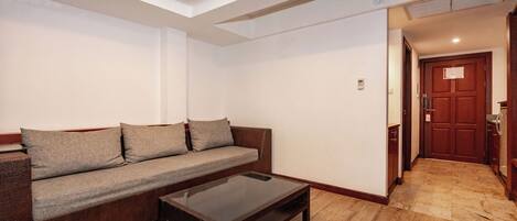 Uma sala de estar com sofá, mesa de centro, piso de madeira e uma porta que dá para outro cômodo.