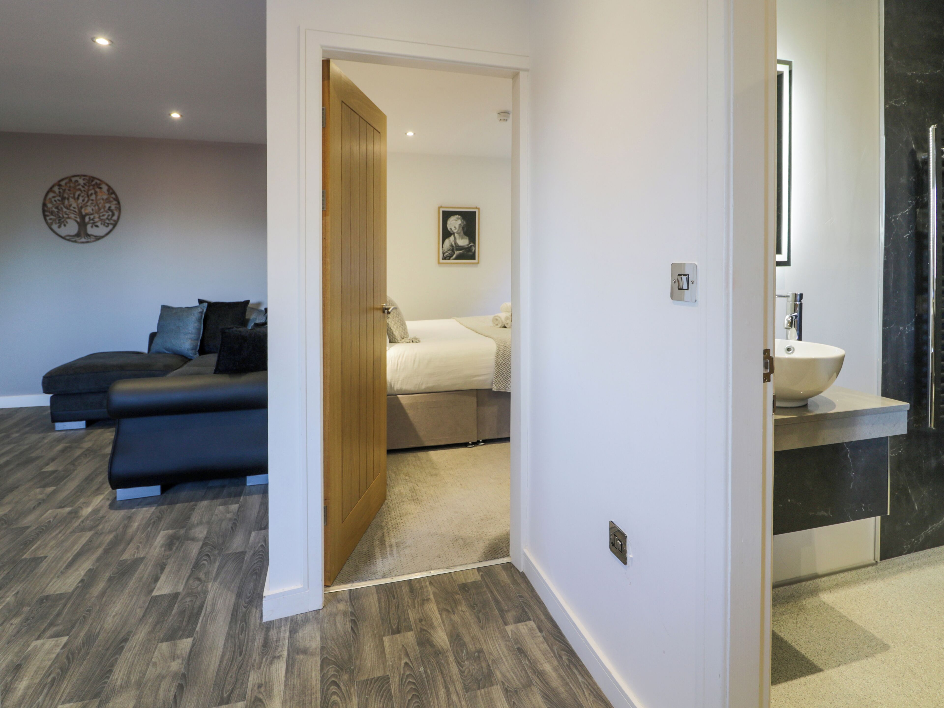 Quarto moderno com cama, porta de madeira e banheiro com pia e espelho.