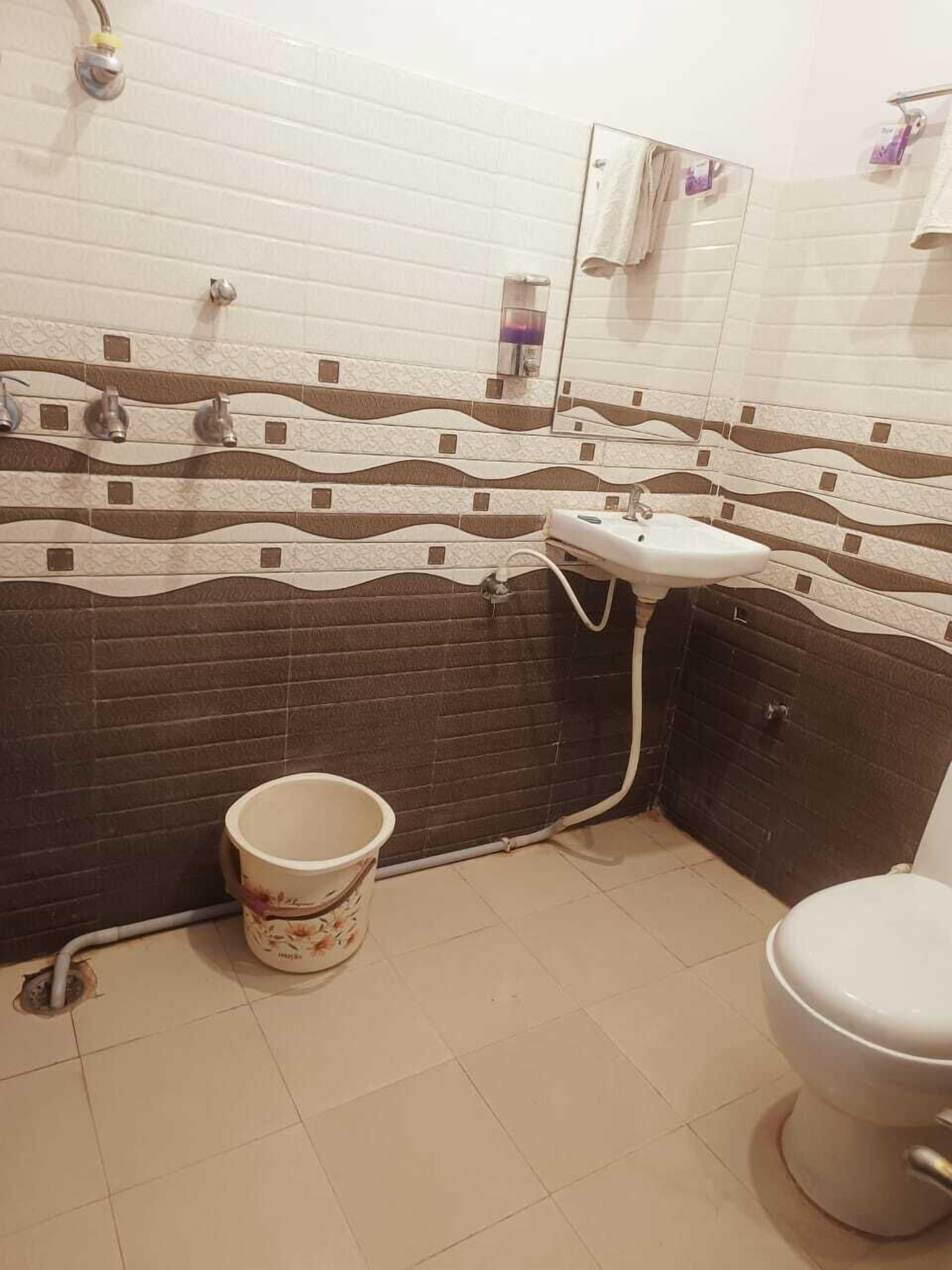 Casa de banho com lavatório branco, sanita e balde.