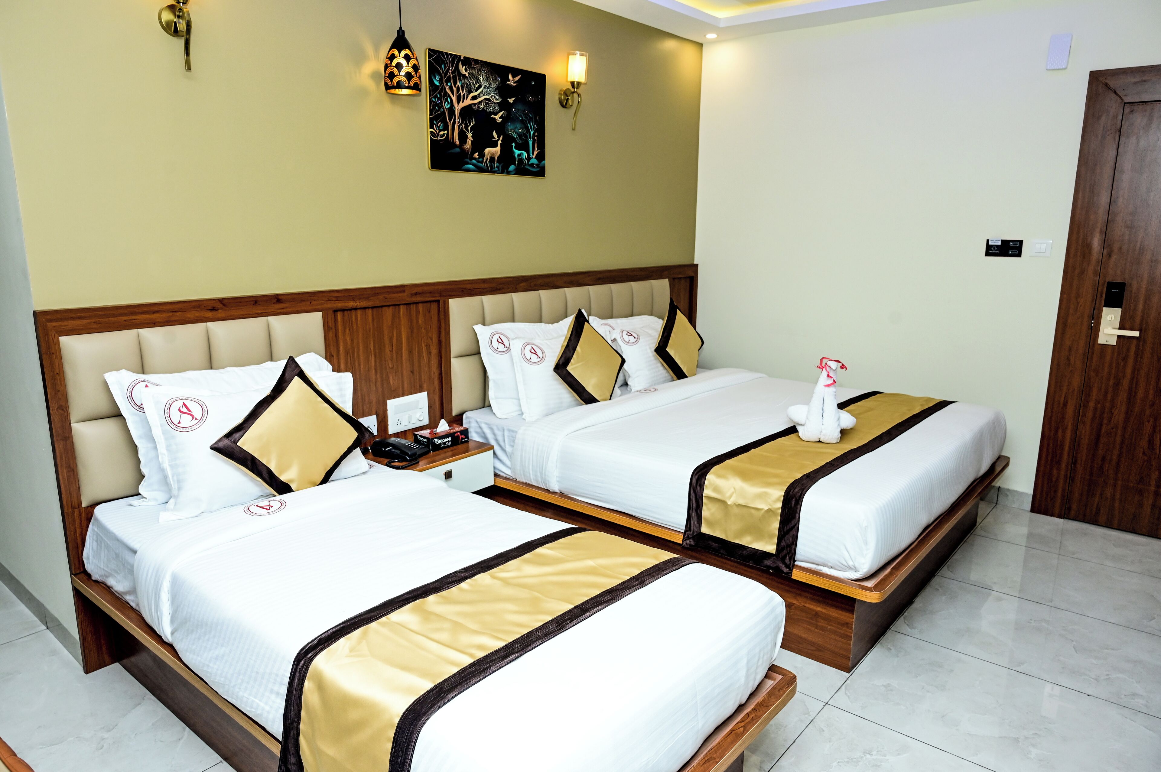 Quarto de hotel com duas camas, cada uma com cabeceira de madeira, roupa de cama branca e almofadas decorativas. Há uma mesa de cabeceira com uma luminária e um telefone.