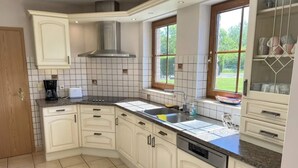 Cozinha com armários brancos, exaustor de aço inoxidável, lava-louças e janela com vista para o verde.
