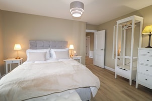 Quarto com uma cama grande, duas mesas de cabeceira com luminárias, um guarda-roupa e uma porta que dá para outro espaço.