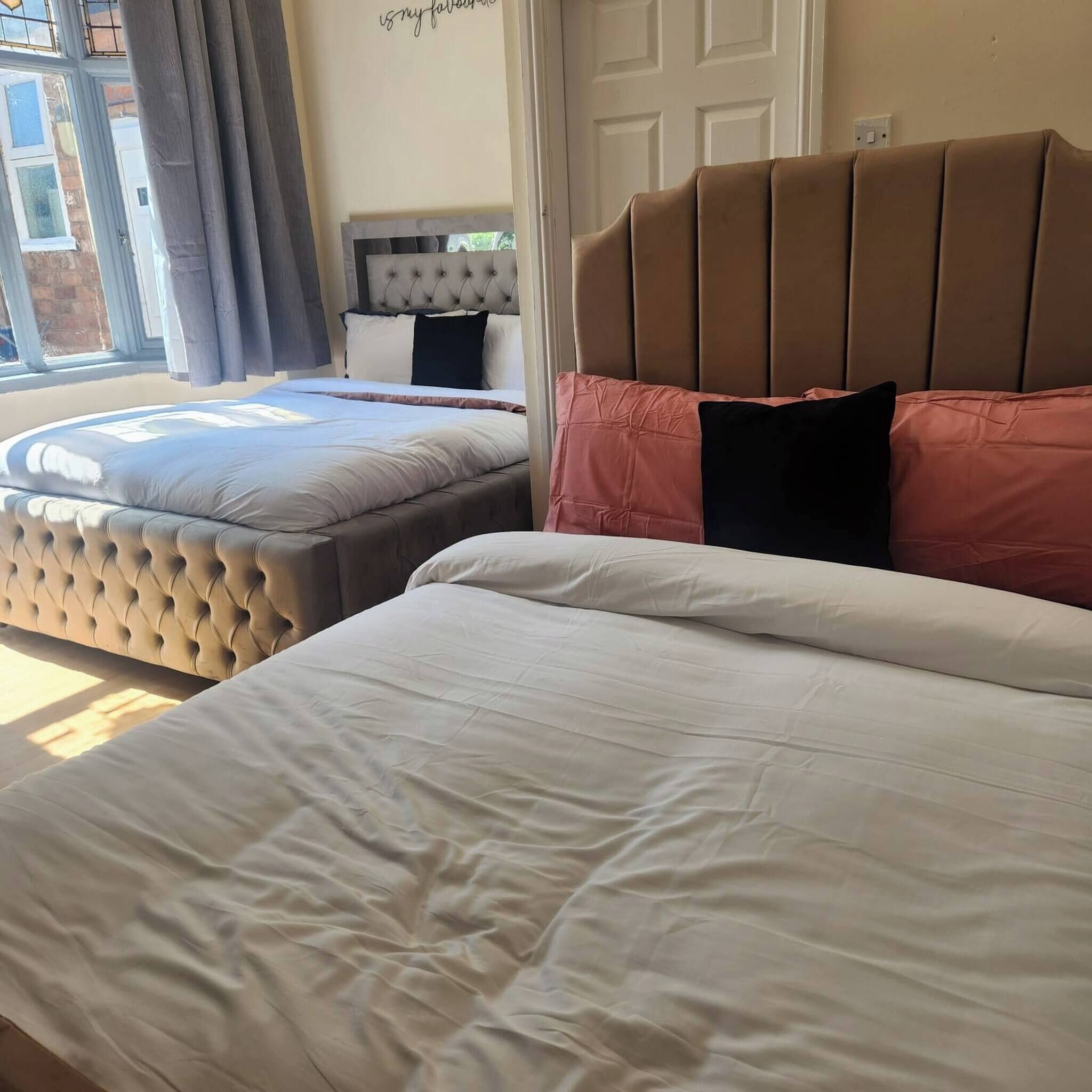 Quarto de hotel com duas camas, uma com cabeceira estofada e outra com cabeceira acolchoada.
