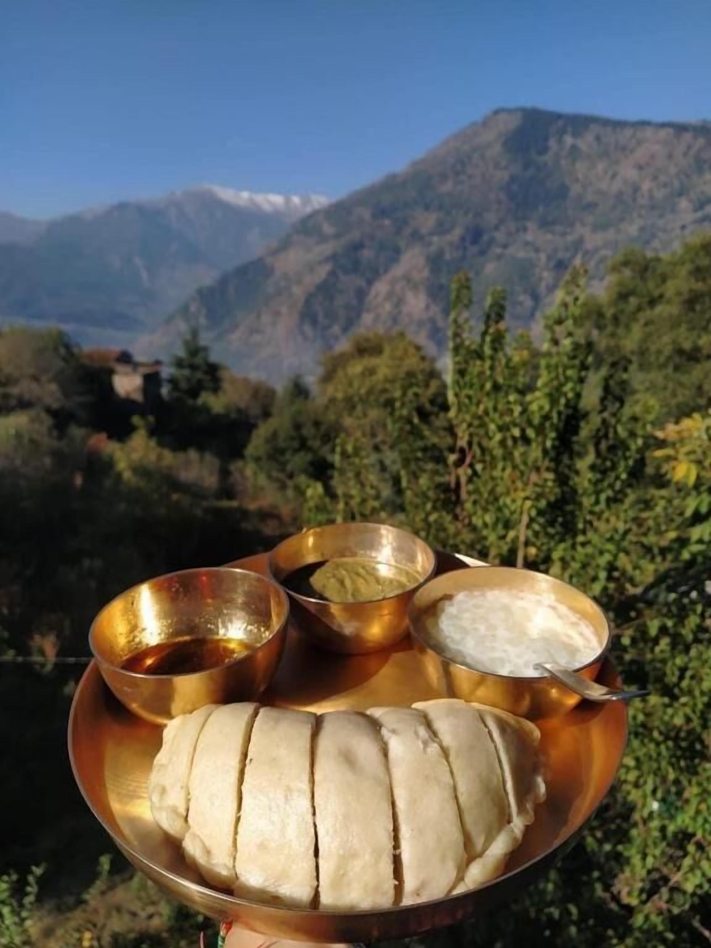 Uma refeição tradicional com pão e chutneys num prato, com montanhas ao fundo.