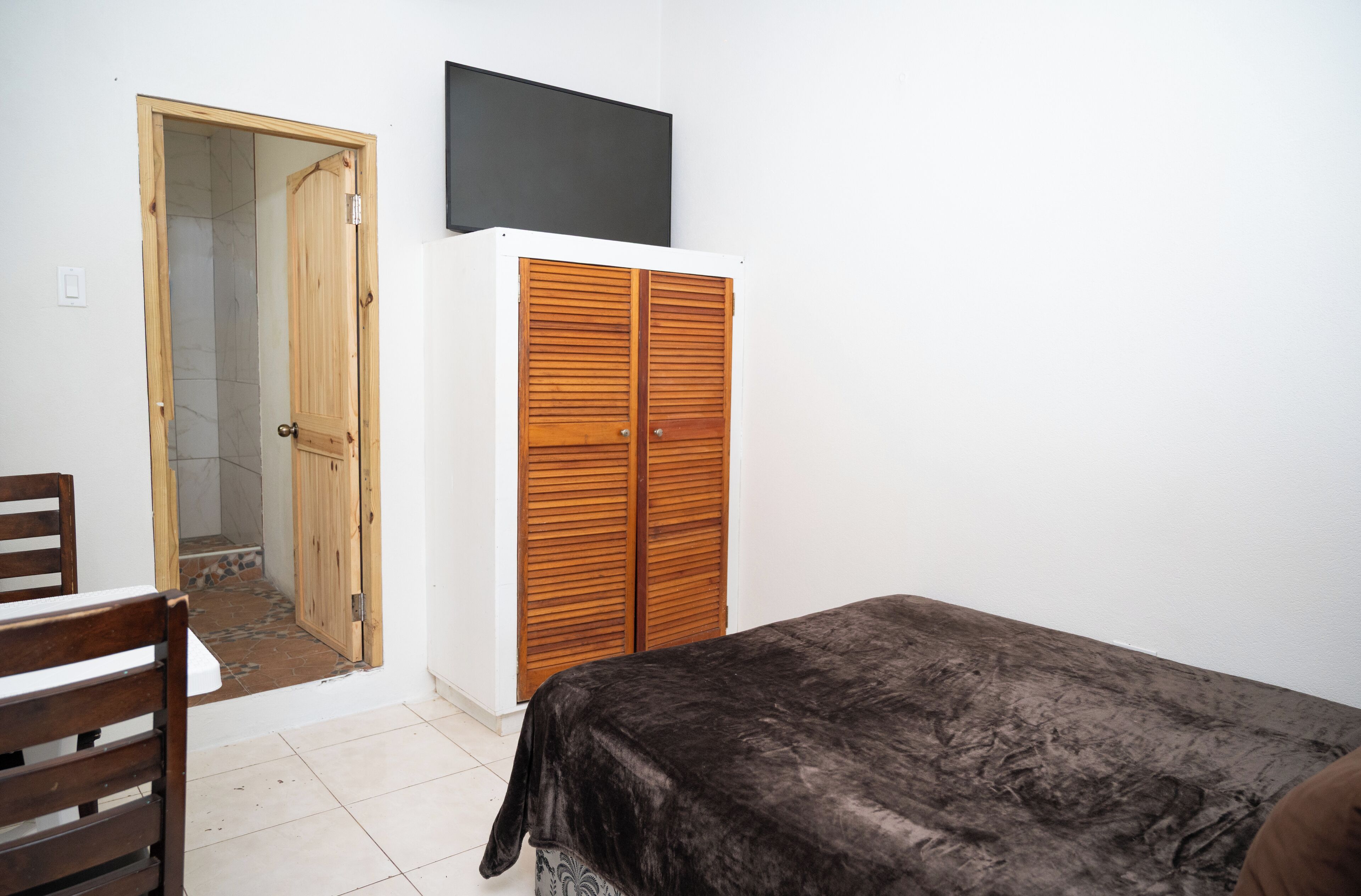 Quarto com cama, guarda-roupa de madeira, porta que dá para um banheiro e televisão de tela plana na parede.