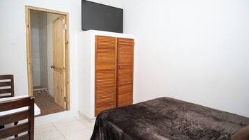 Quarto com cama, guarda-roupa de madeira, porta que dá para um banheiro e televisão de tela plana na parede.