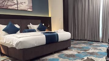 Quarto de hotel com uma cama grande, cabeceira, obra de arte na parede, janela com cortinas e um tapete estampado.