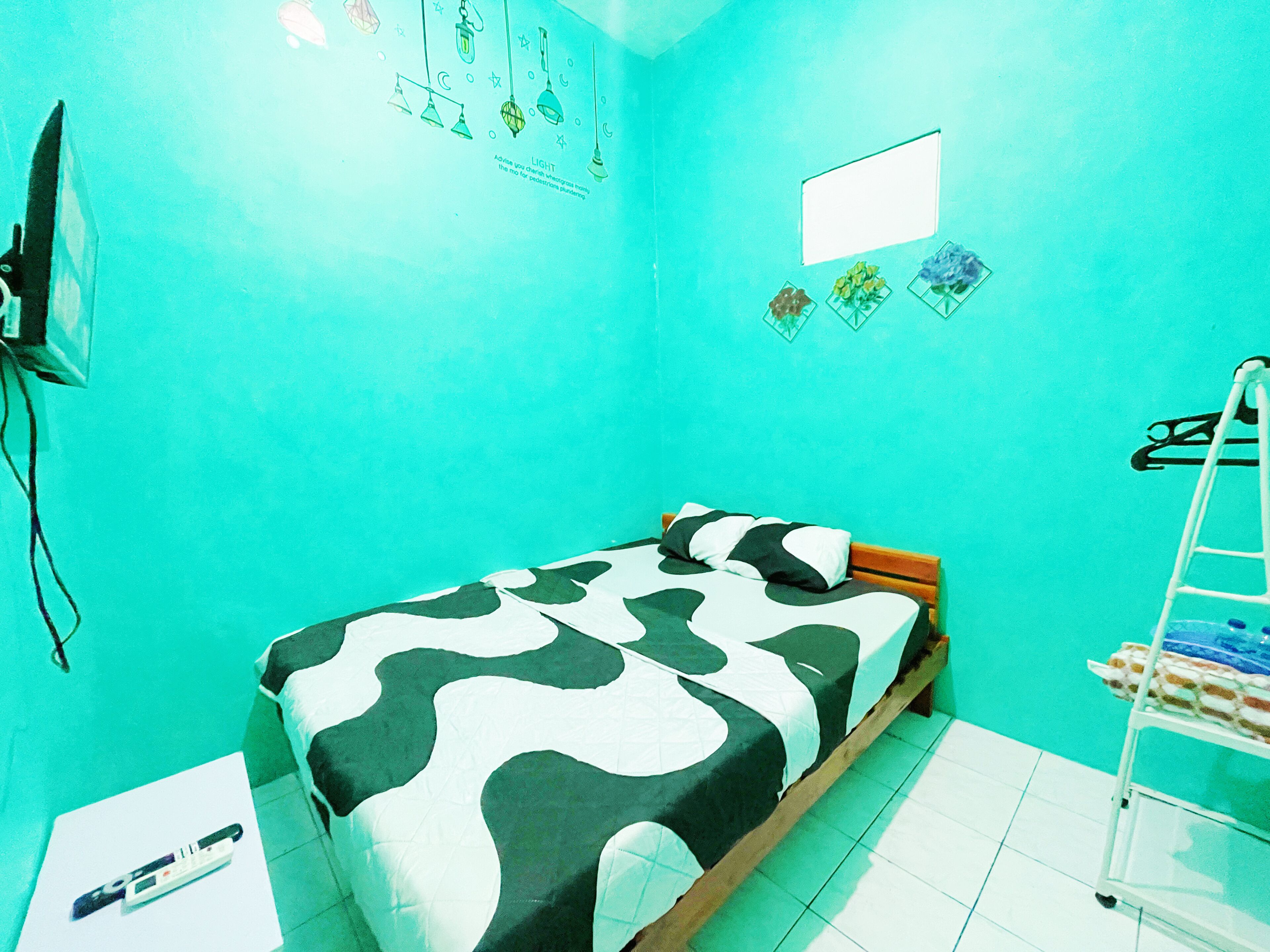Quarto com paredes verde-água, cama com colcha estampada em preto e branco, uma lousa e uma escada com objetos em cima.