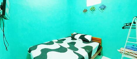 Quarto com paredes verde-água, cama com colcha estampada em preto e branco, uma lousa e uma escada com objetos em cima.