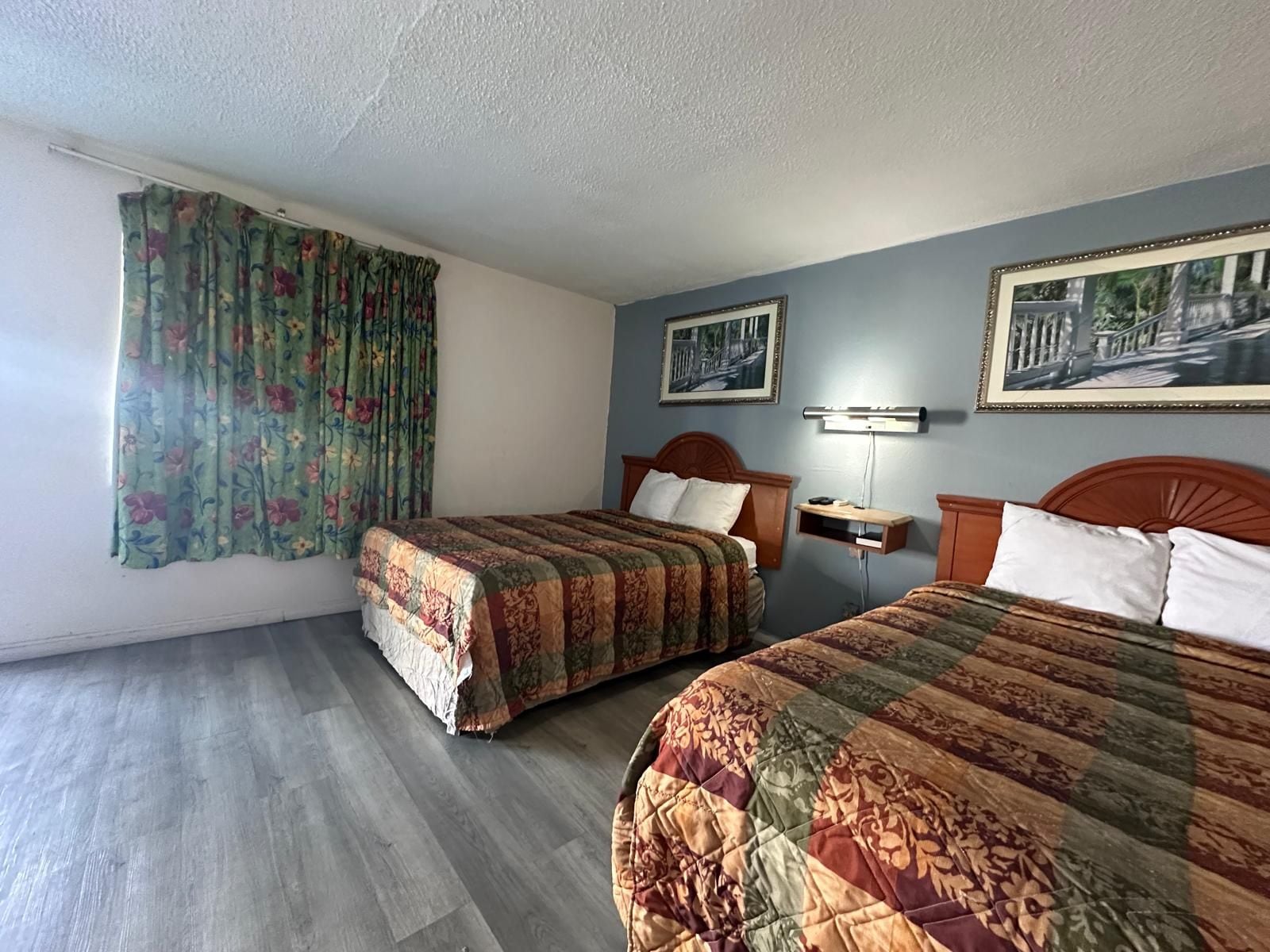 Quarto de hotel com duas camas, uma mesa de cabeceira, uma luminária e duas fotos emolduradas na parede.