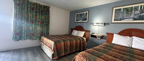 Quarto de hotel com duas camas, uma mesa de cabeceira, uma luminária e duas fotos emolduradas na parede.