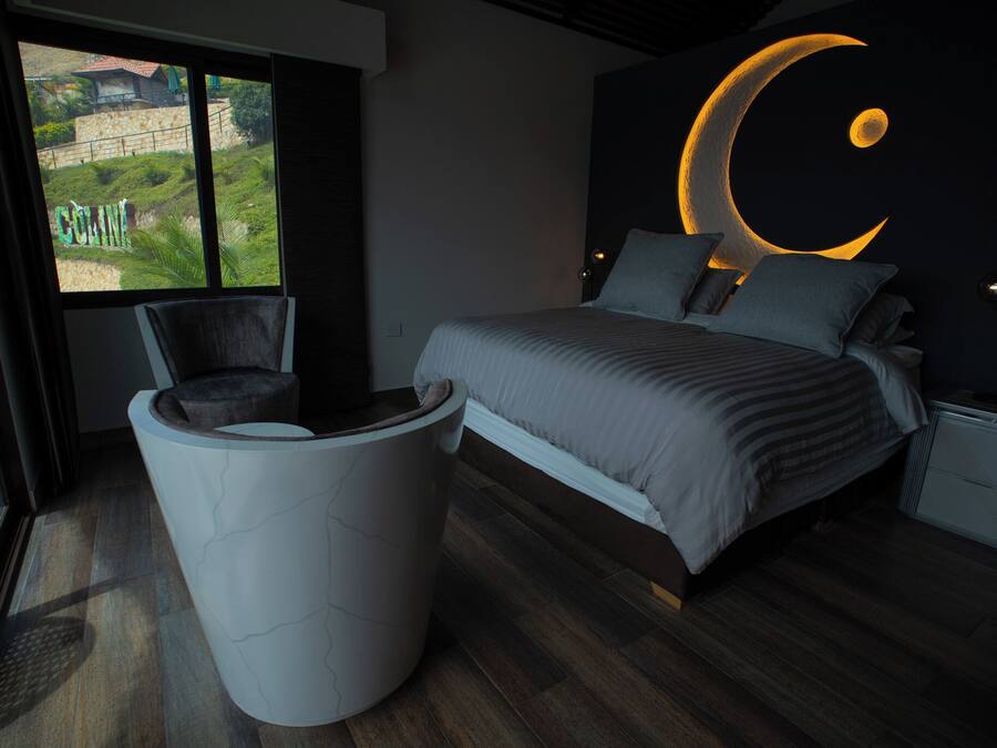 Quarto moderno com uma cama grande, área de estar curvada e vista para um jardim através de uma janela.