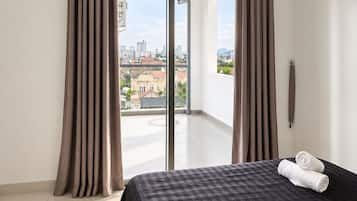 Quarto de hotel com cama, cortinas, vista para a cidade e varanda.