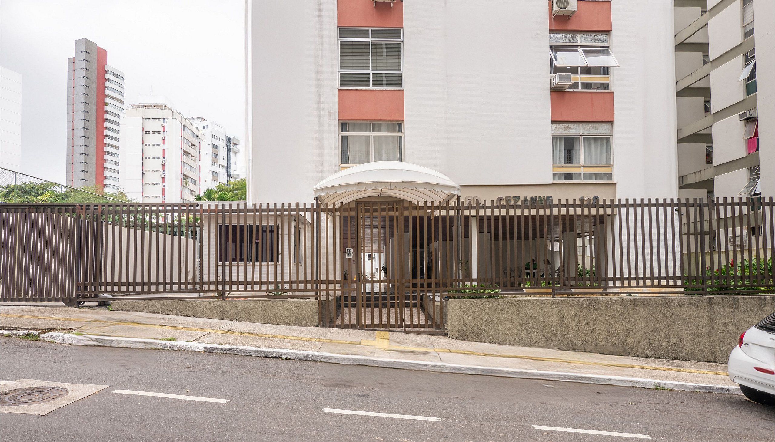 Uma entrada com portão para um edifício de fachada branca e detalhes vermelhos.