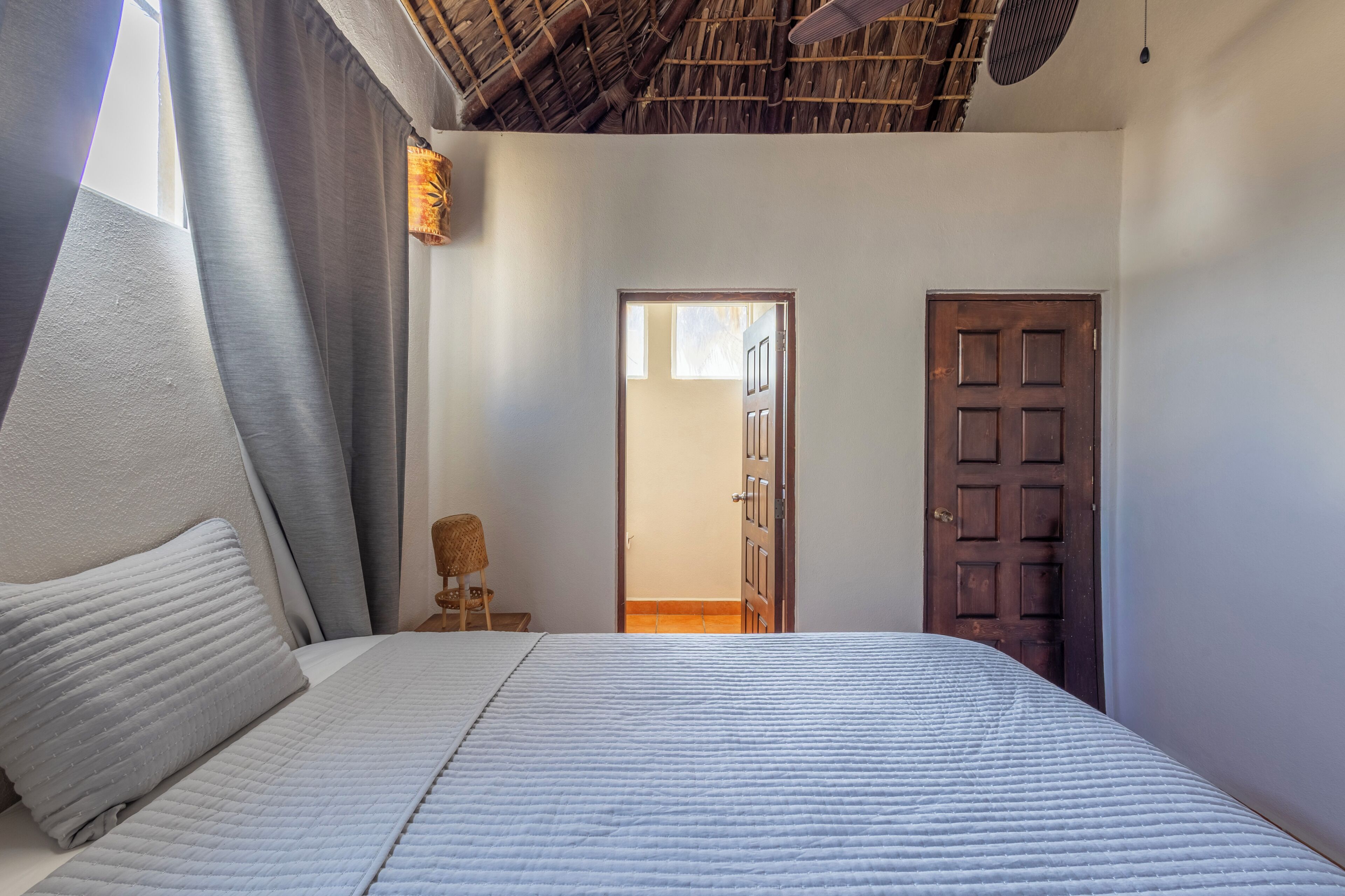 Um quarto com uma cama, uma porta de madeira e vista para um corredor.