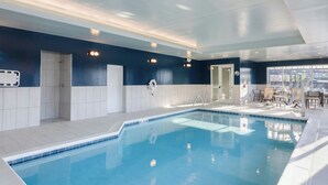 Piscina interna com chão em mosaico, esquema de cores azul e branco, e área de estar com cadeiras e mesas.
