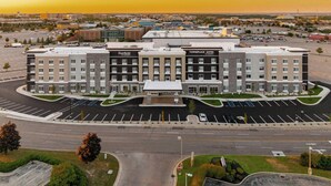 Hotel de vários andares com entrada central, estacionamento e vista para a paisagem urbana ao redor.