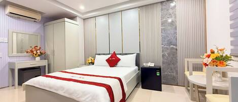 Quarto de hotel moderno com cama bem arrumada, mesa de cabeceira com telefone, escrivaninha com cadeira e uma janela grande com cortinas.