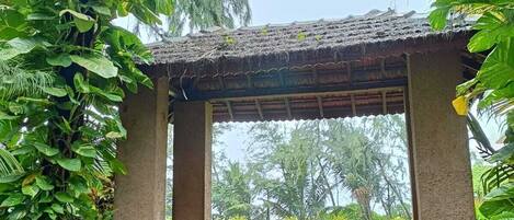 Uma construção rústica de pedra com telhado de palha, rodeada por vegetação exuberante e um jardim bem cuidado.