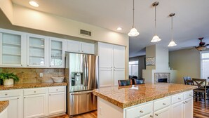 Uma cozinha moderna com armários brancos, bancadas de granito, eletrodomésticos de aço inoxidável e iluminação pendente.
