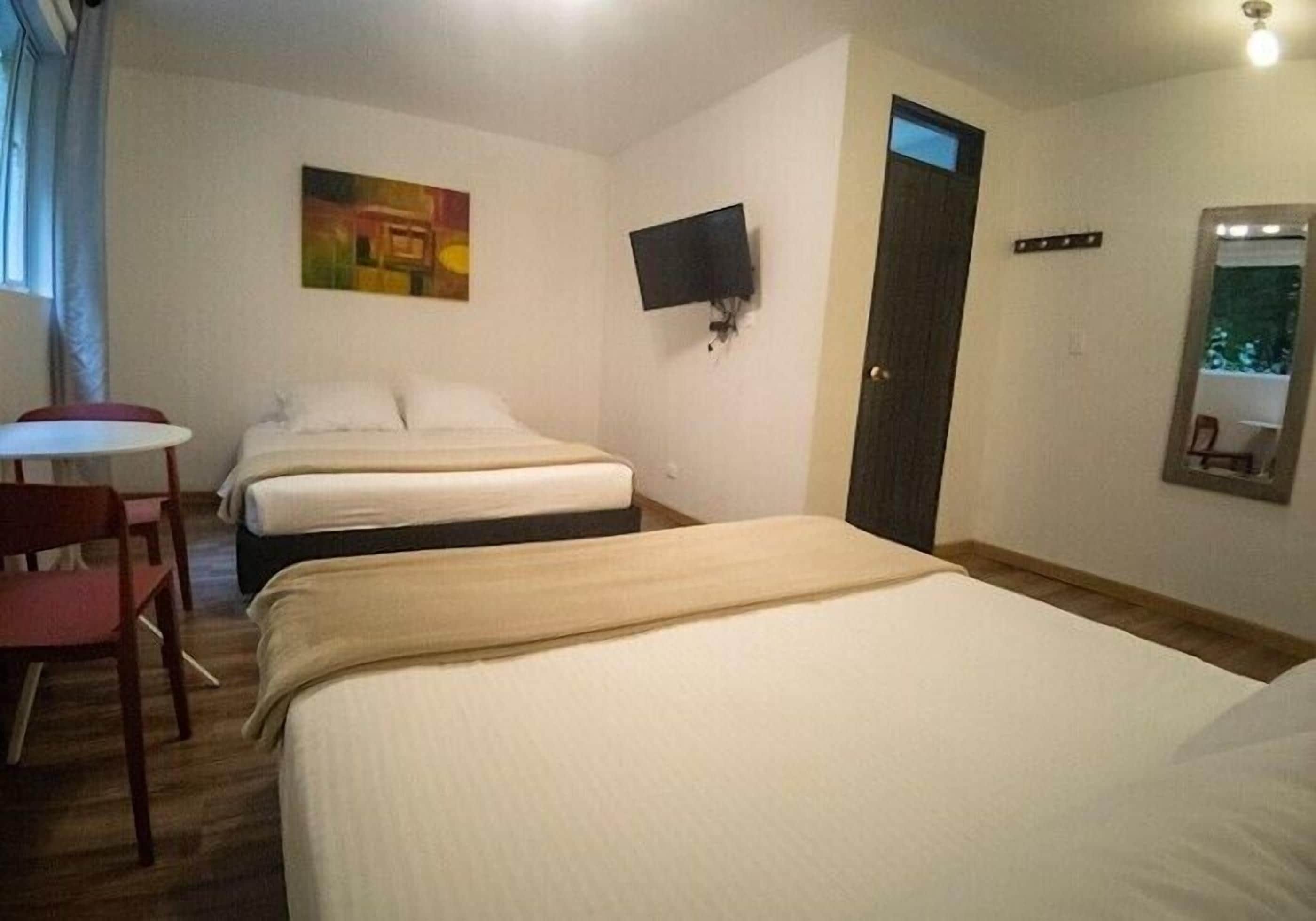 Quarto de hotel com duas camas, uma TV fixada na parede, uma mesinha e uma cadeira.