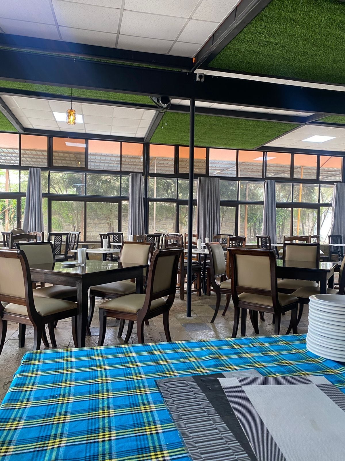 Restaurante com área externa, mesas, cadeiras e vista para o verde.