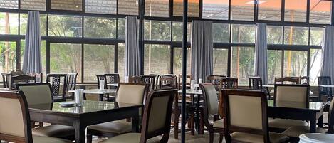 Restaurante com área externa, mesas, cadeiras e vista para o verde.