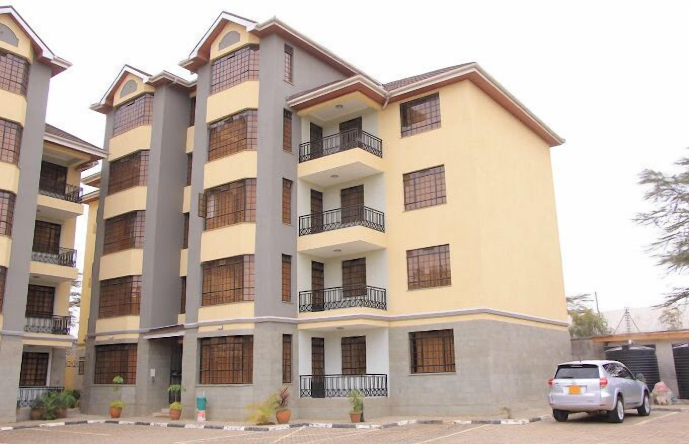 Um edifício residencial com várias andares, varandas, área de estacionamento e plantas em vasos.