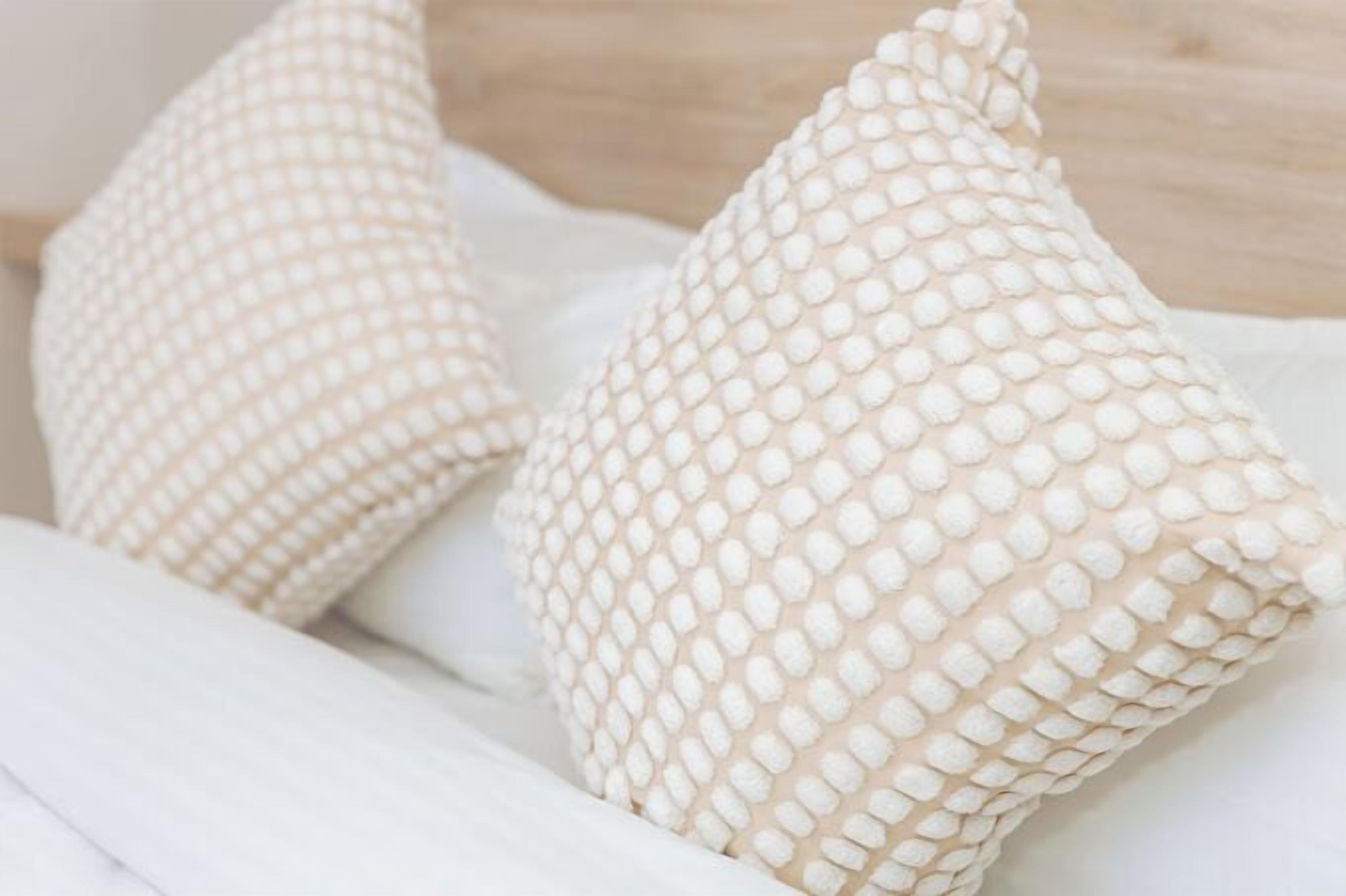 Duas almofadas texturizadas sobre uma cama com cabeceira de madeira.