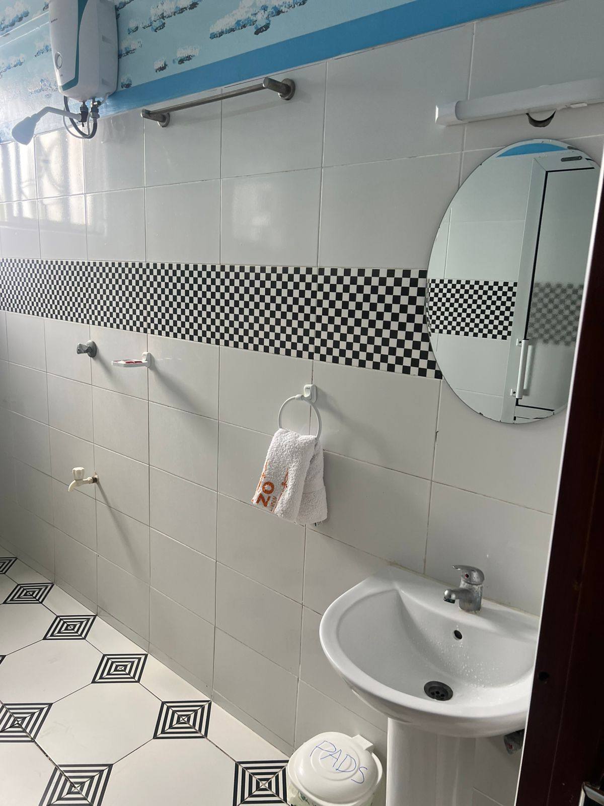 Casa de banho com lavatório branco, um porta-toalhas com toalha, espelho e chão estampado.