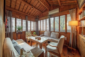 Quarto aconchegante com paredes e teto de madeira, um sofá, cadeiras, uma mesa e uma estante de livros.
