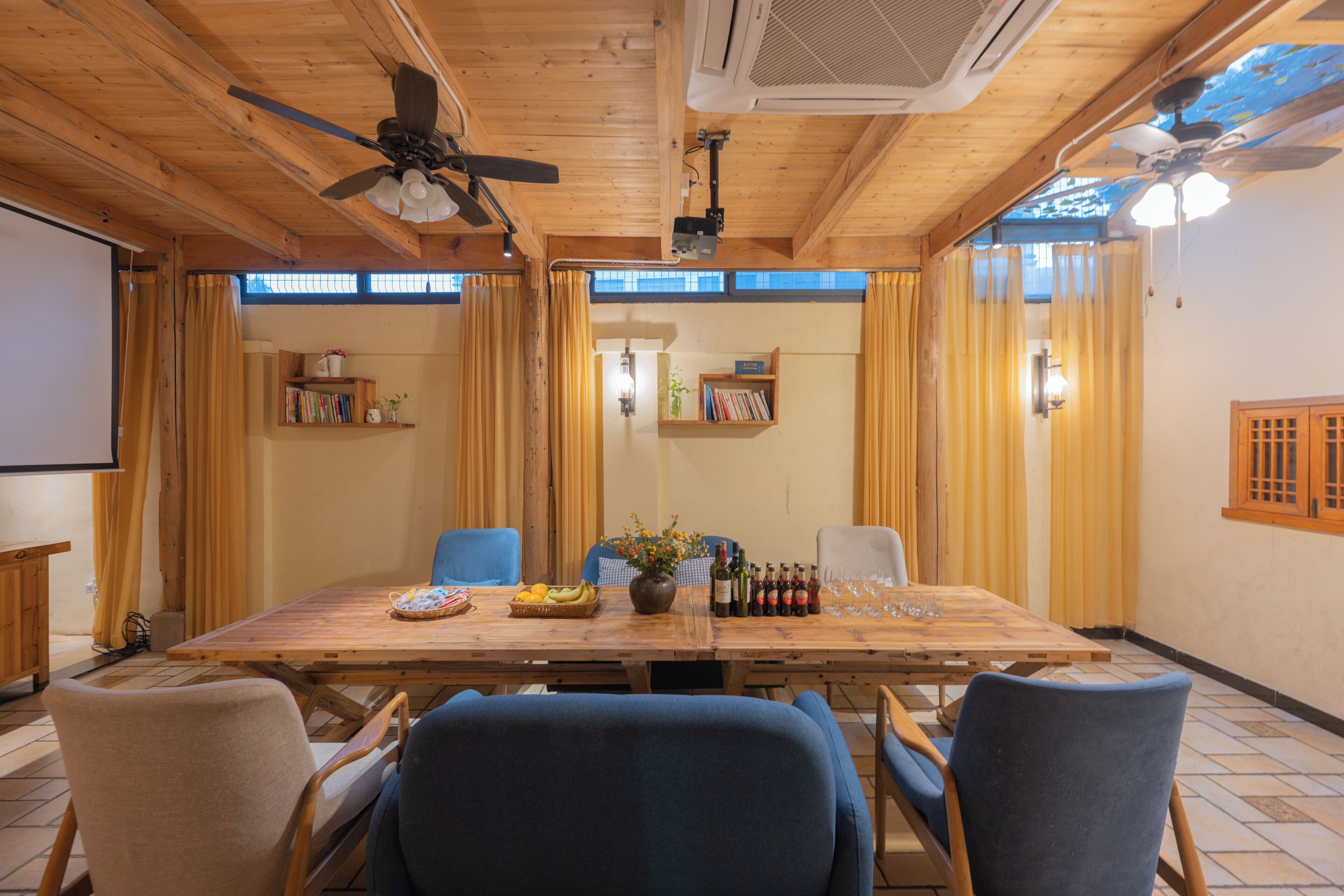 Um quarto com painéis de madeira, uma mesa grande, cadeiras, ventiladores de teto e uma tela de projeção.