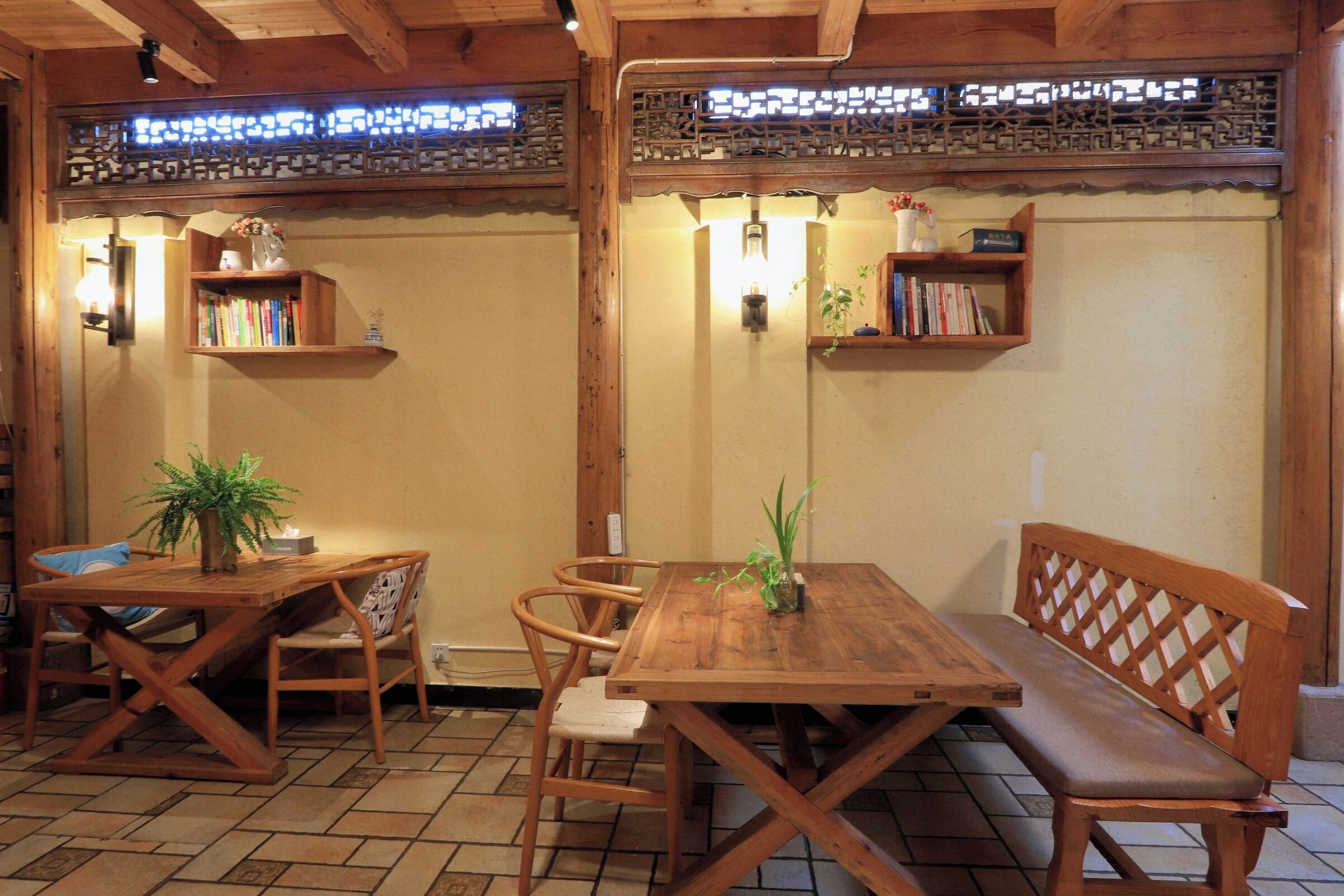 Interior em madeira com mesa de jantar, cadeiras e um banco. Estantes com livros e objetos decorativos fixadas nas paredes.