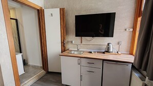 Uma cozinha compacta com bancada de madeira, pia embutida, pequena geladeira e televisão na parede.