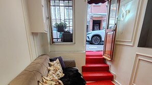 Um hall de hotel com um sofá bege, carpete vermelho e vista para a rua.