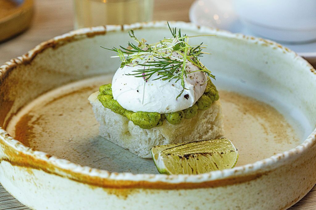 Prato com uma porção de creme e cobertura verde, decorado com ervas, acompanhado de uma fatia de limão.