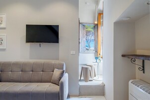 Uma sala de estar moderna com sofá, televisão de tela plana, pintura de paisagem costeira e uma pequena mesa com banquinhos.