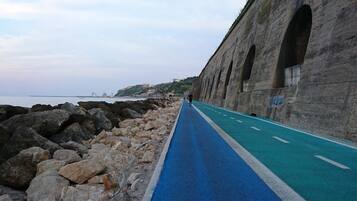Uma estrada costeira com ciclovia azul, grandes muros de pedra e uma orla rochosa.