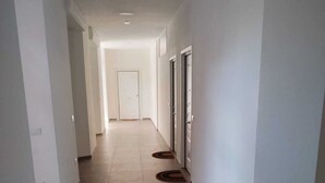 Um corredor com piso de azulejos, paredes brancas e portas em ambos os lados.